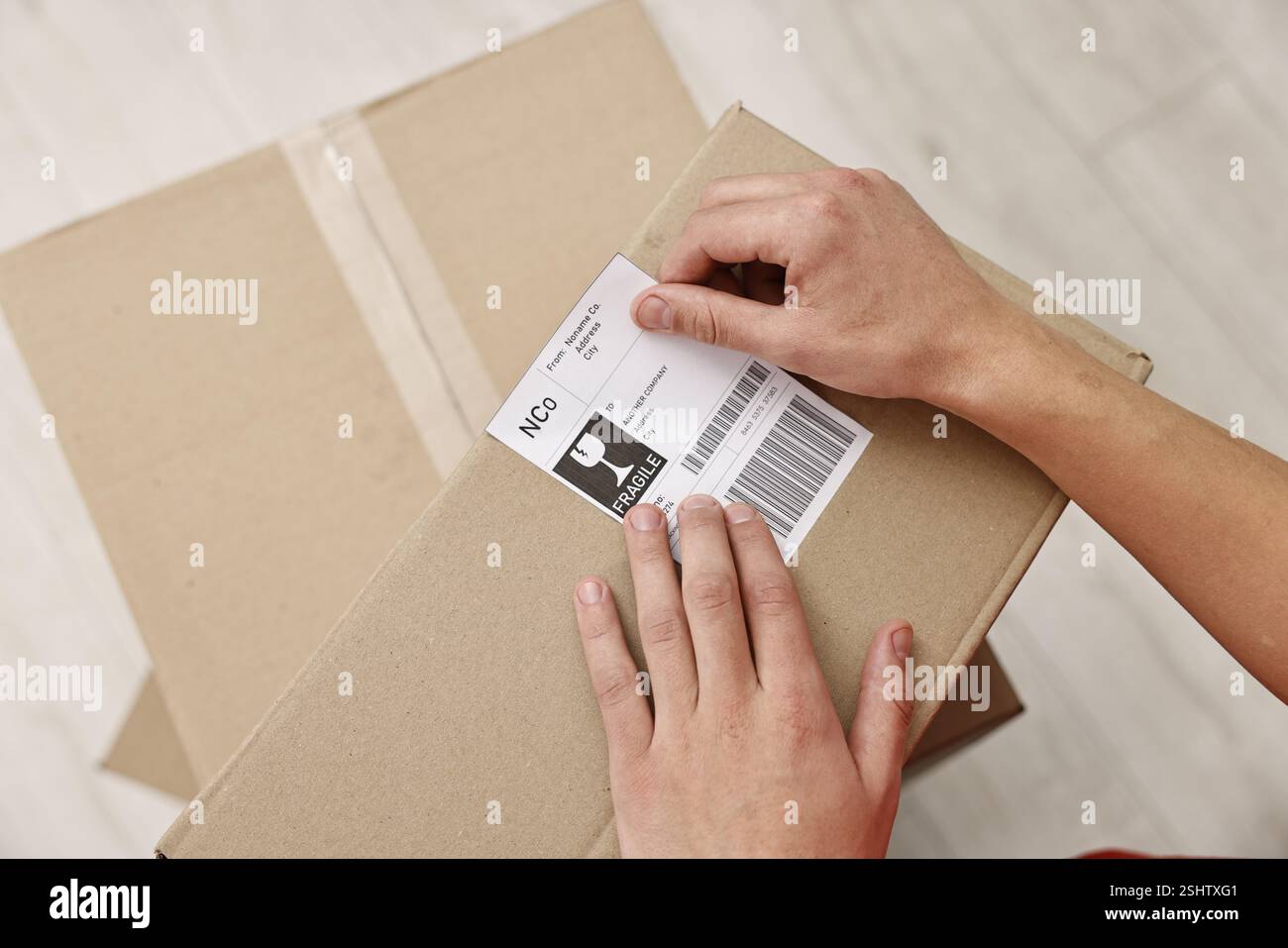 Man sticking shipping label with barcode on parcel indoors, above view ...