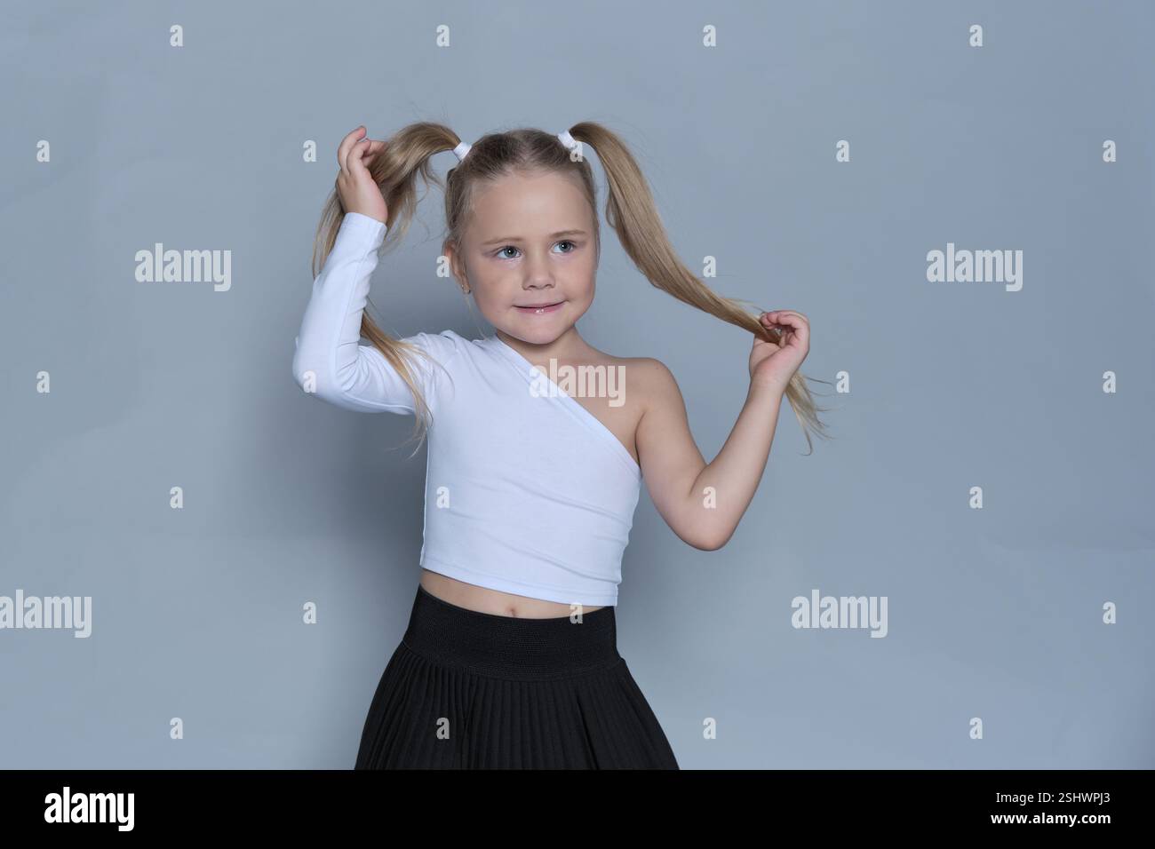 Happy girl holding her pigtails, beaming with joy in a white sleeve top ...