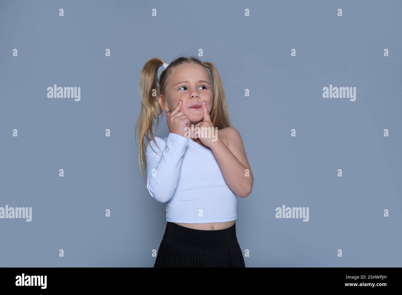 A little girl puffs her cheeks, hands playfully pressing her face ...