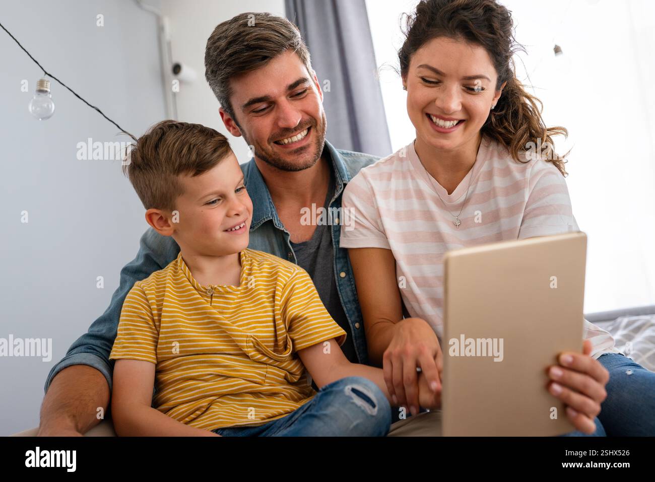 Happy family with kid having fun using tablet together, parents and child laughing relaxing at ...