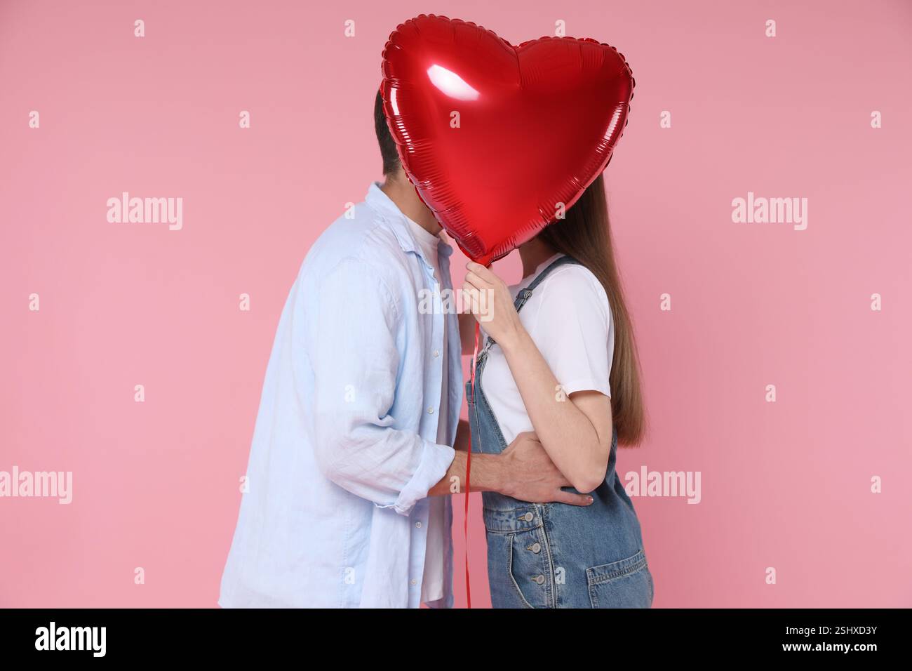 Lovely couple kissing behind heart shaped balloon on pink background ...
