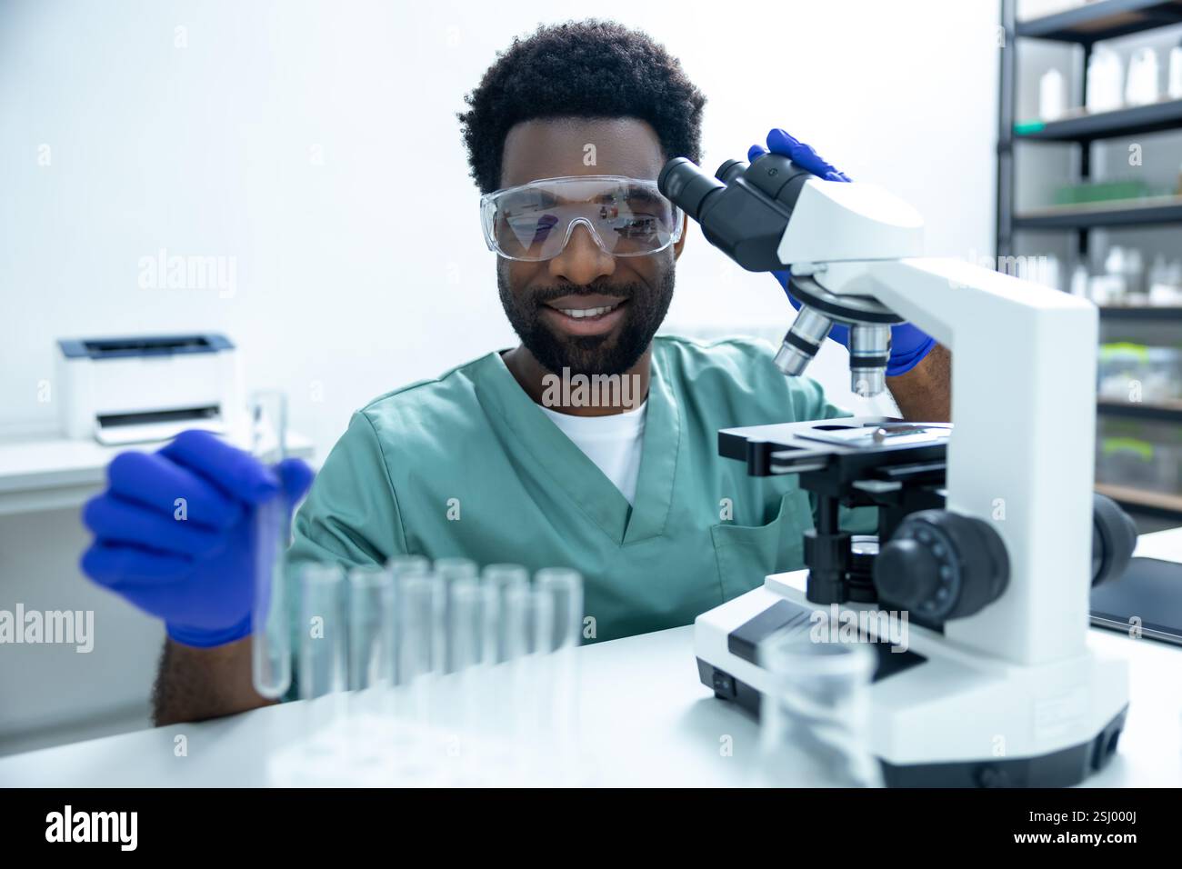 Male scientist looking under microscope and using test tubes Stock ...