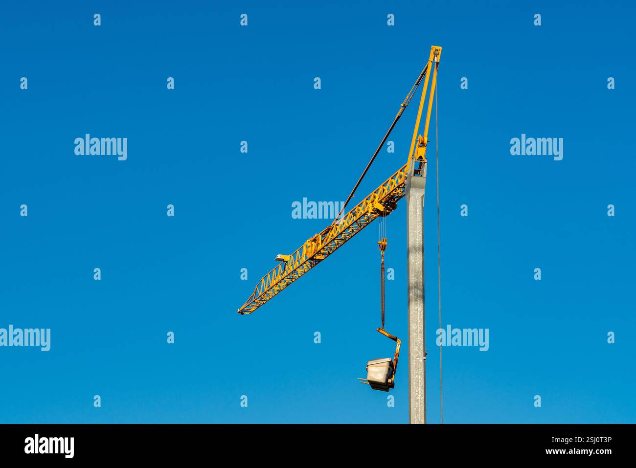 A tall construction crane stands against a bright blue sky, with its ...