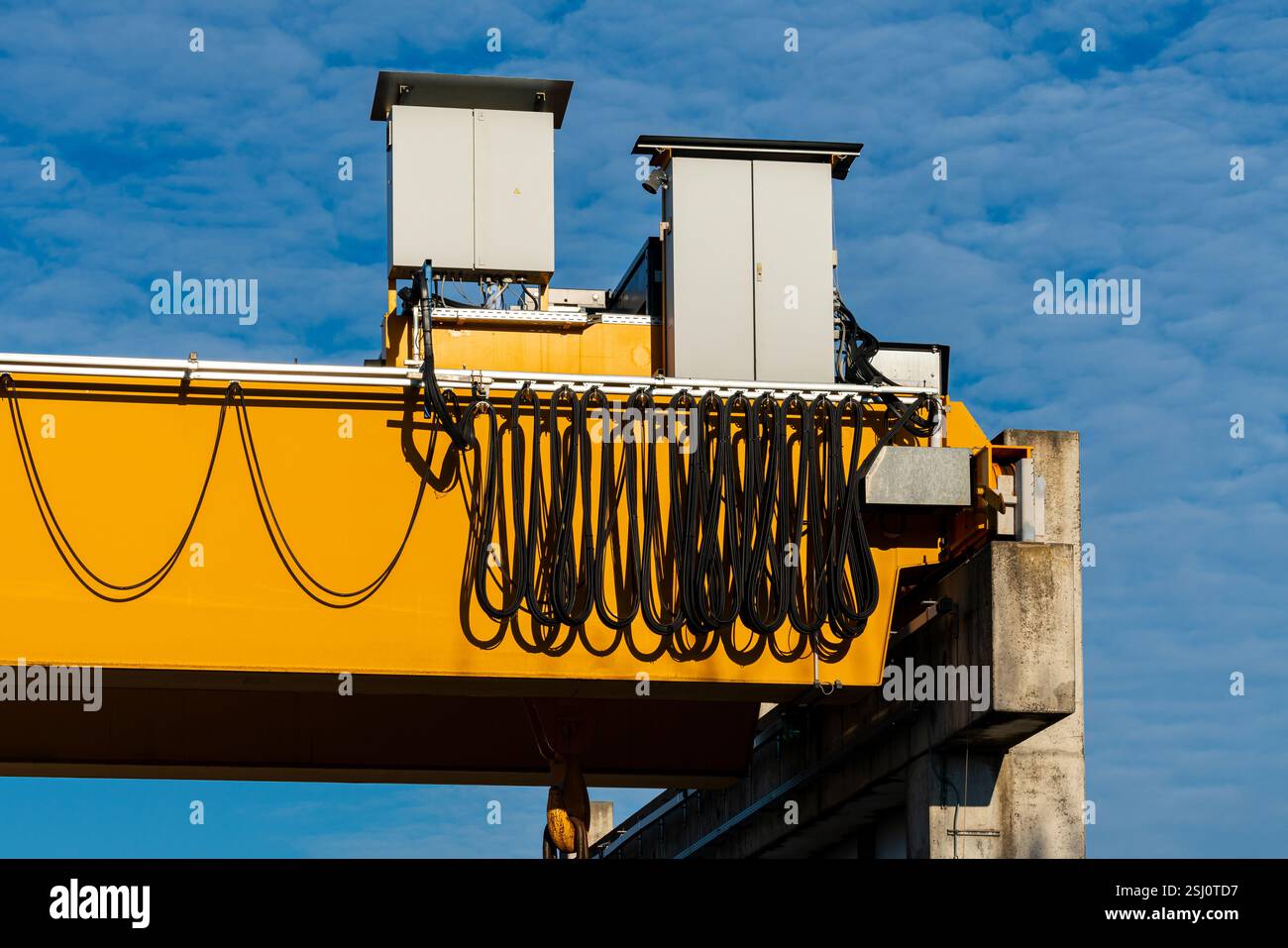 Heavy yellow overhead crane with coiled cables and power boxes at a ...