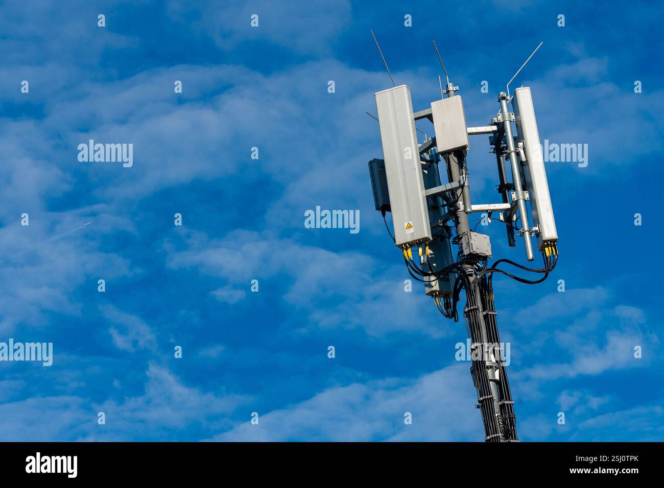 A tall cell tower rises prominently against a vibrant blue sky filled ...