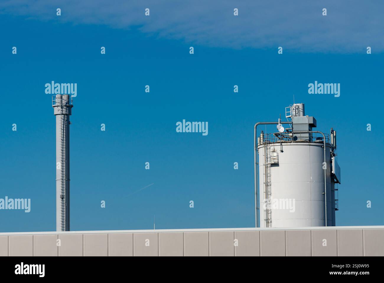 Tall industrial structures rise against a clear blue sky, showcasing a smokestack and a large ...