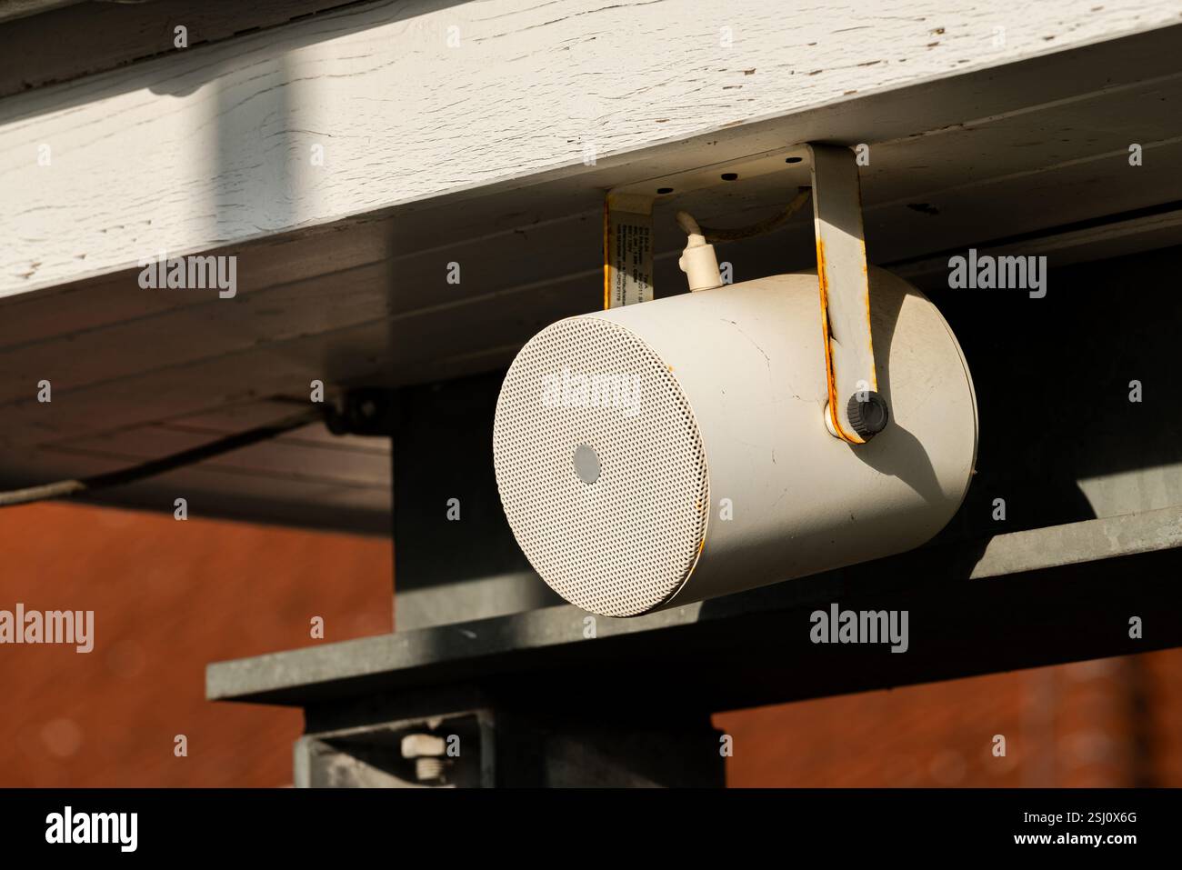 A round outdoor speaker is securely mounted on a wooden beam ...