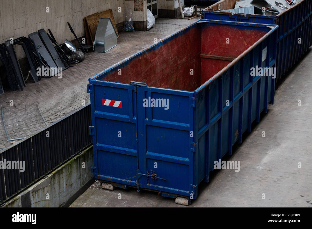 A large blue dumpster stands empty in an urban setting, surrounded by ...