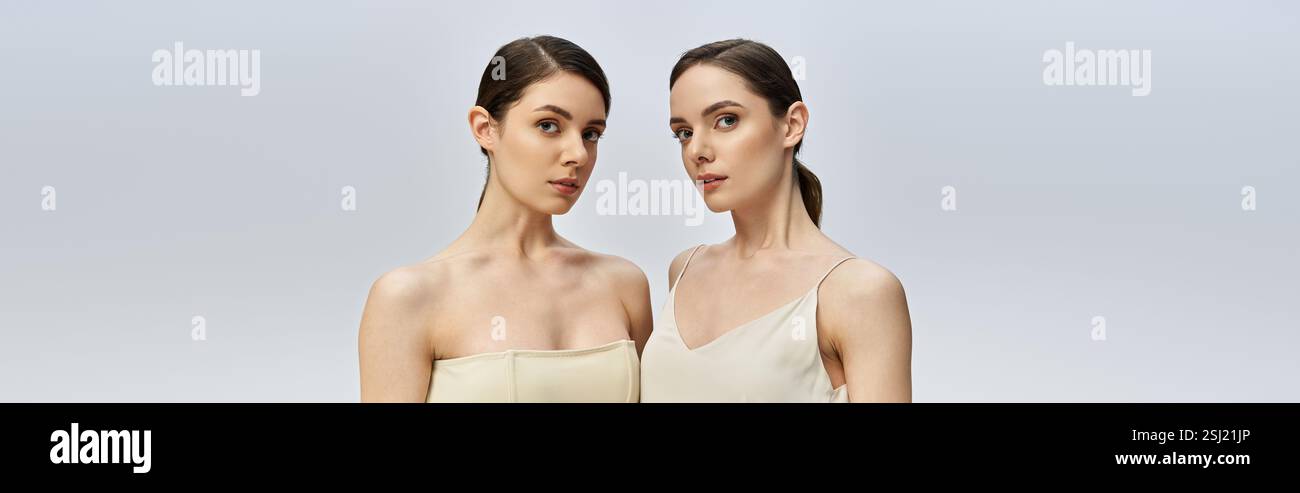 Two charming twin sisters stand side by side in a minimalist setting ...