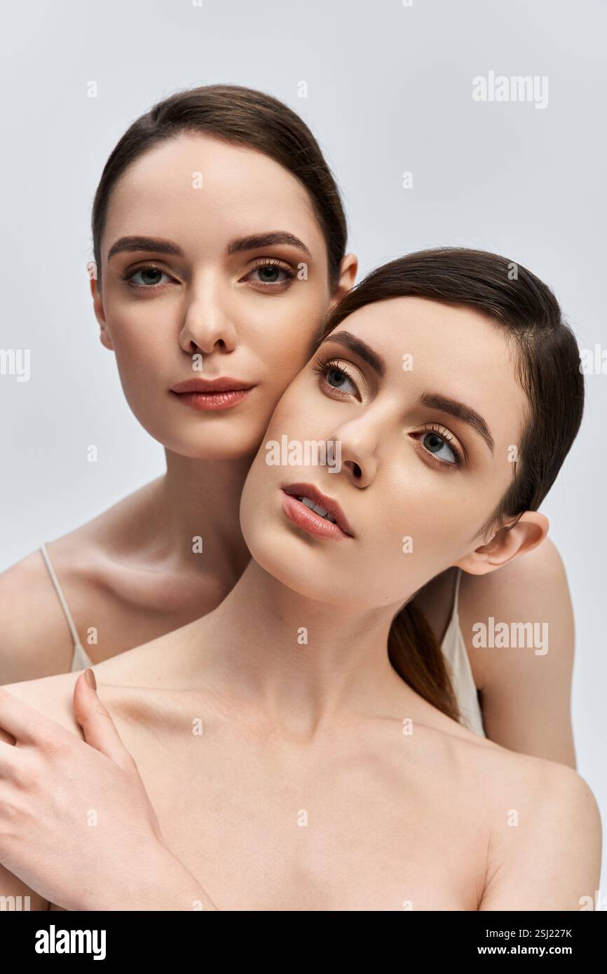 Two stunning twin sisters exhibit elegance and poise in a minimalist backdrop, radiating warmth ...