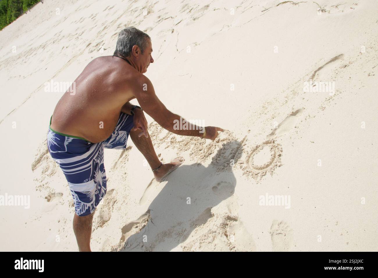 A man writes on the beach sand, Bahamas. The sun shines brightly ...