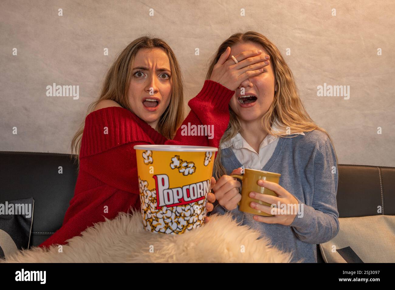 Two friends are watching a horror movie on television, eating popcorn ...