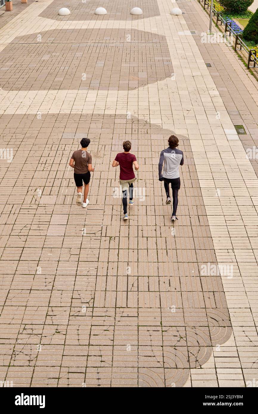 Three male athletes are jogging outdoors in a modern urban environment ...