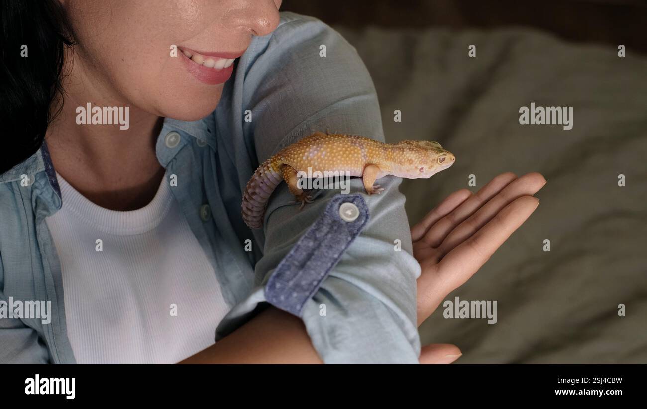 A close-up of a smiling woman interacting with a gecko on her arm. The ...