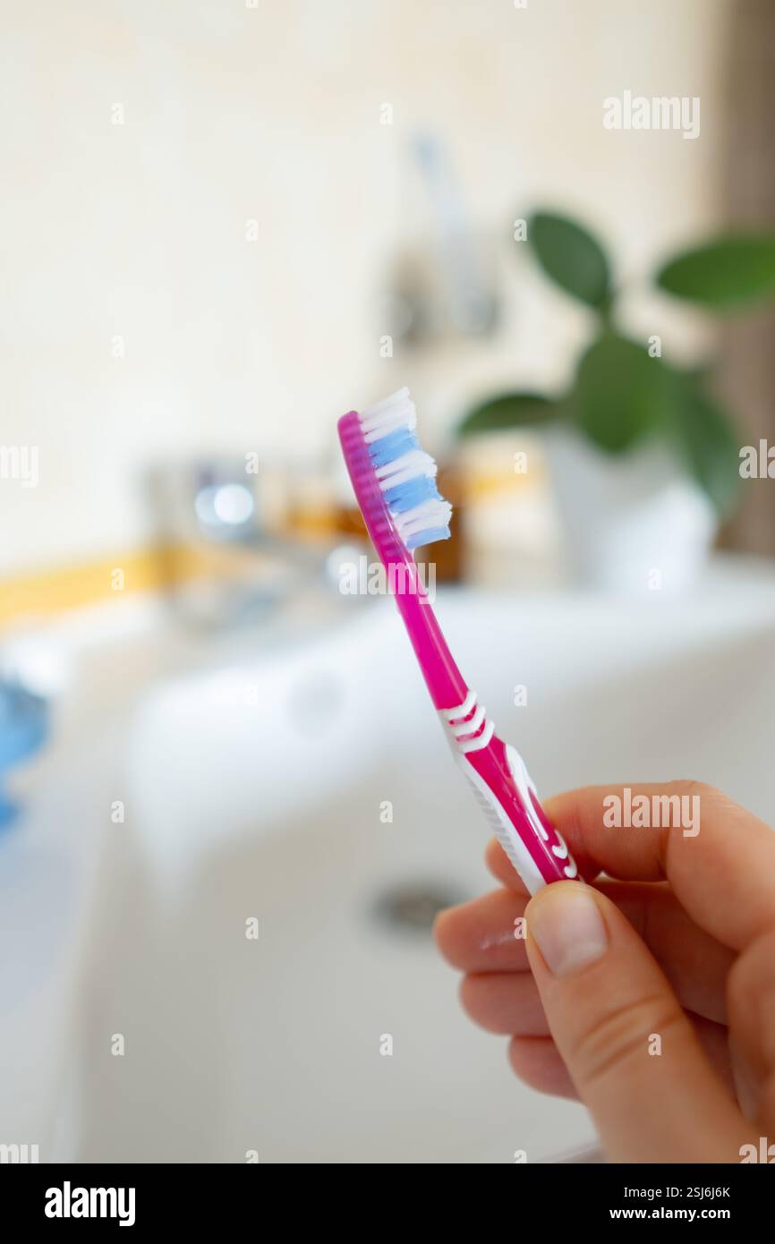 Hand holds pink toothpaste by the sink in the bathroom. Hands with ...