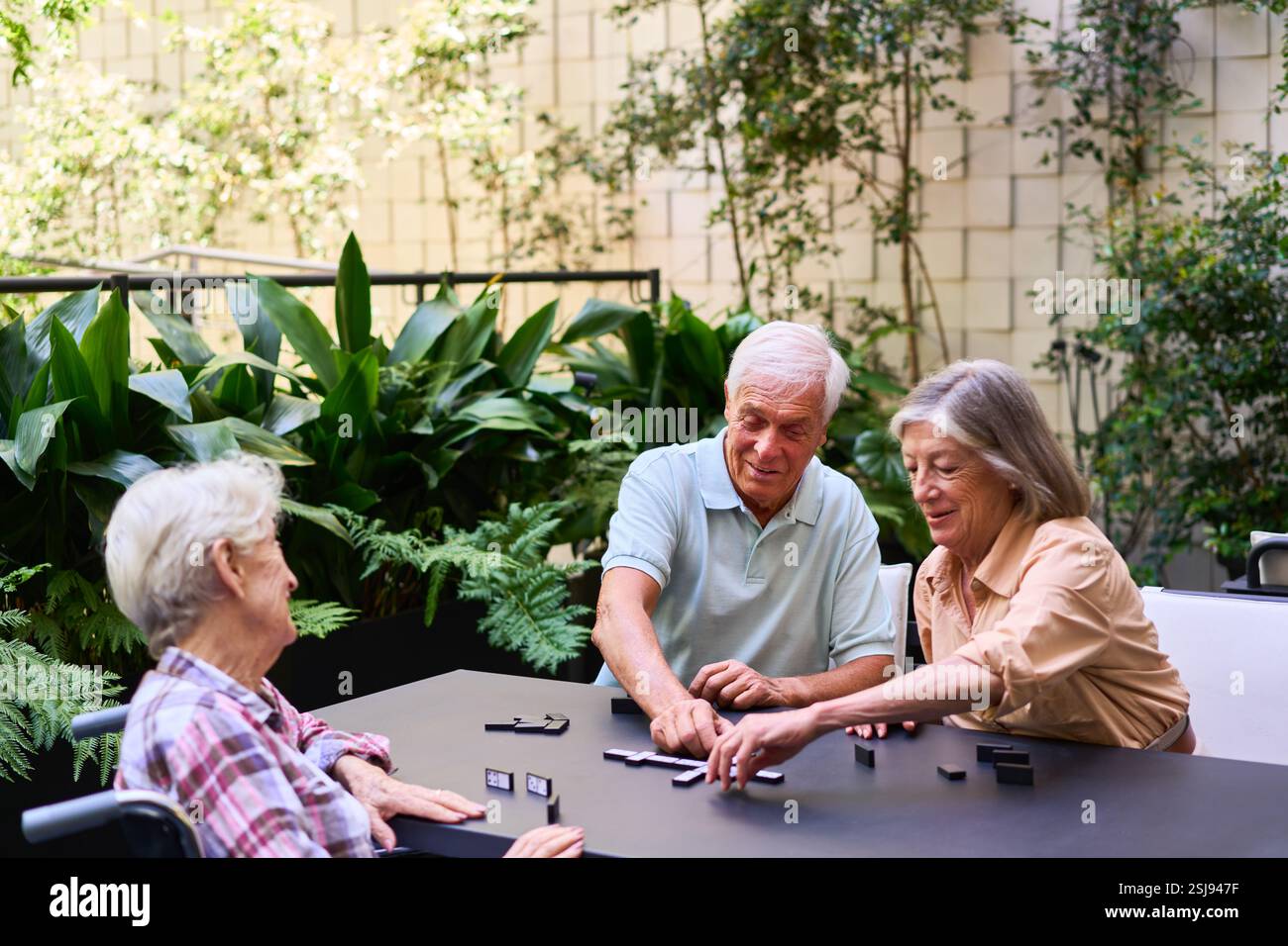 Group of three senior individuals playing a board game at a table ...