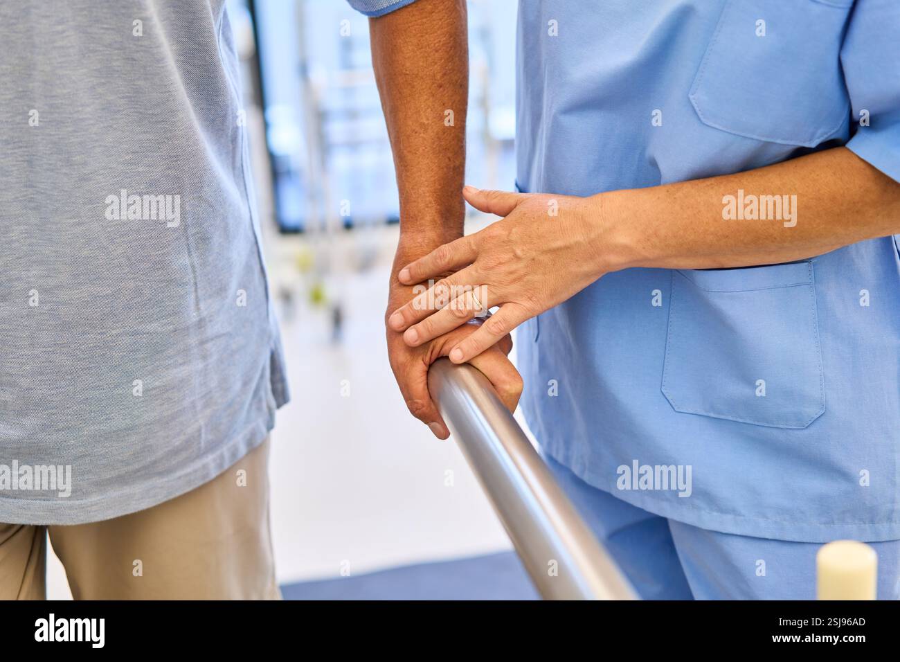 A caregiver supports a senior individual's hand over a rail in a ...