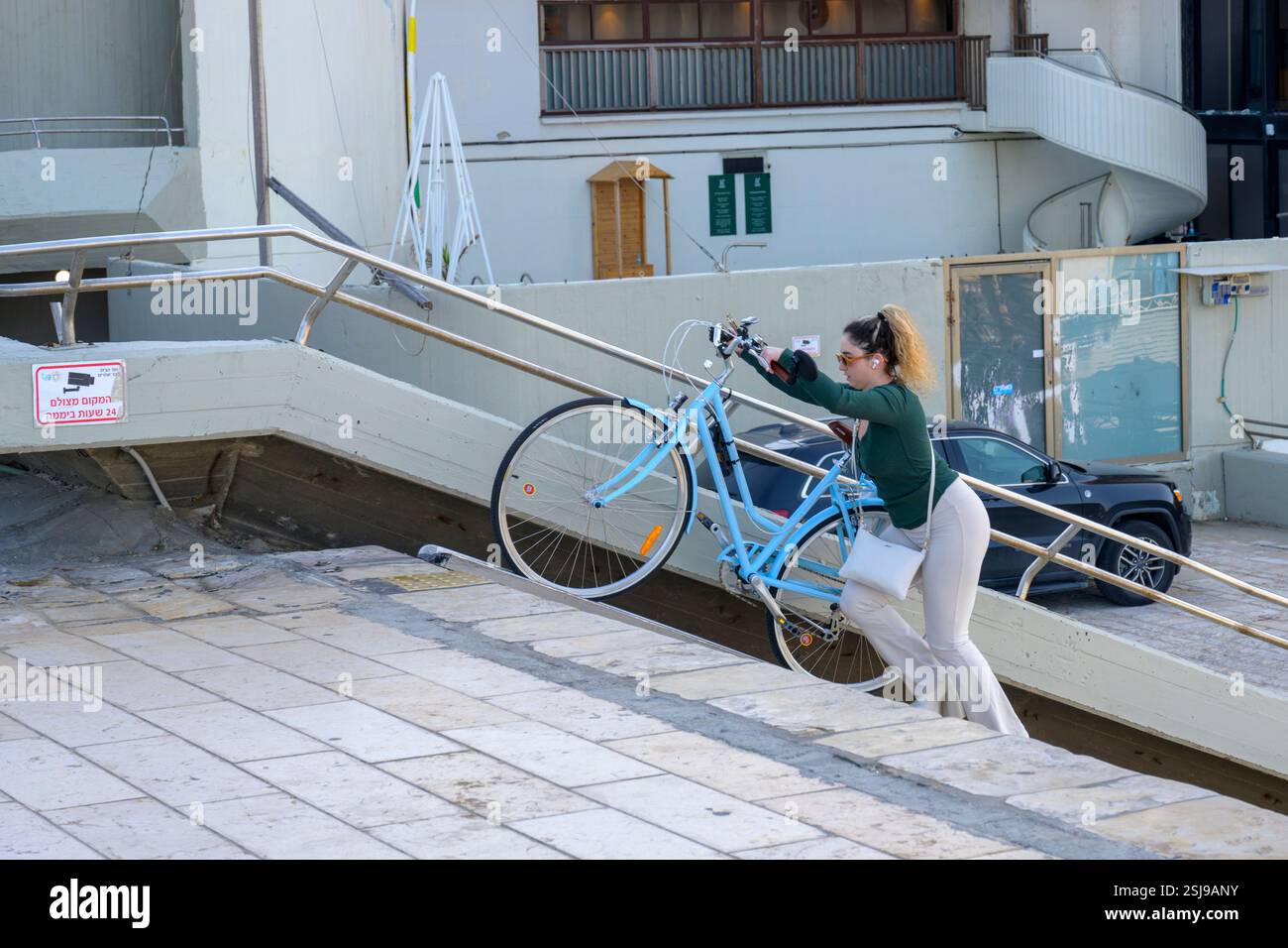 A young woman pushes her bicycle up the stairs using a inclined bike ...