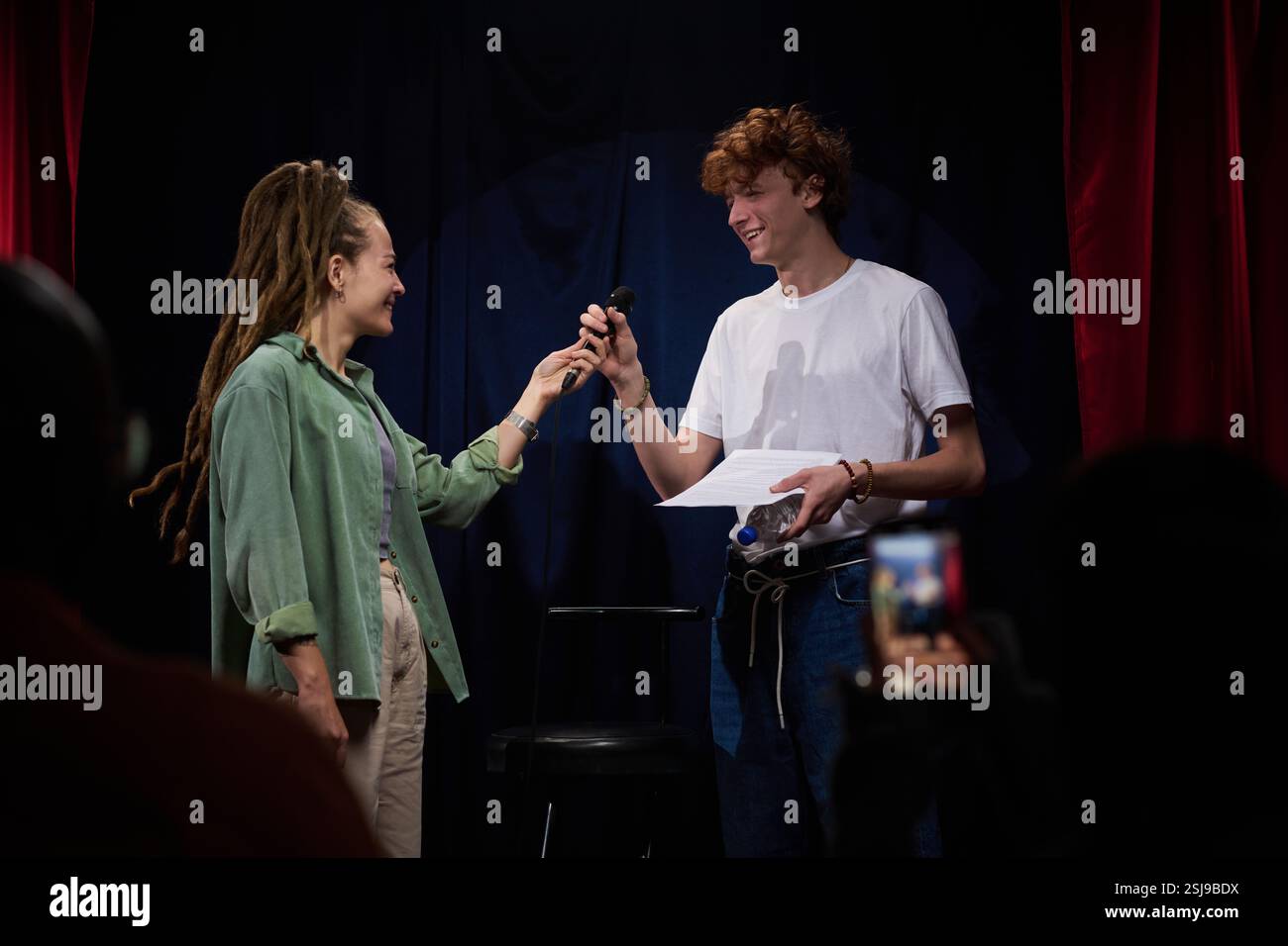Two people engaging in an interaction on stage, with one person handing ...