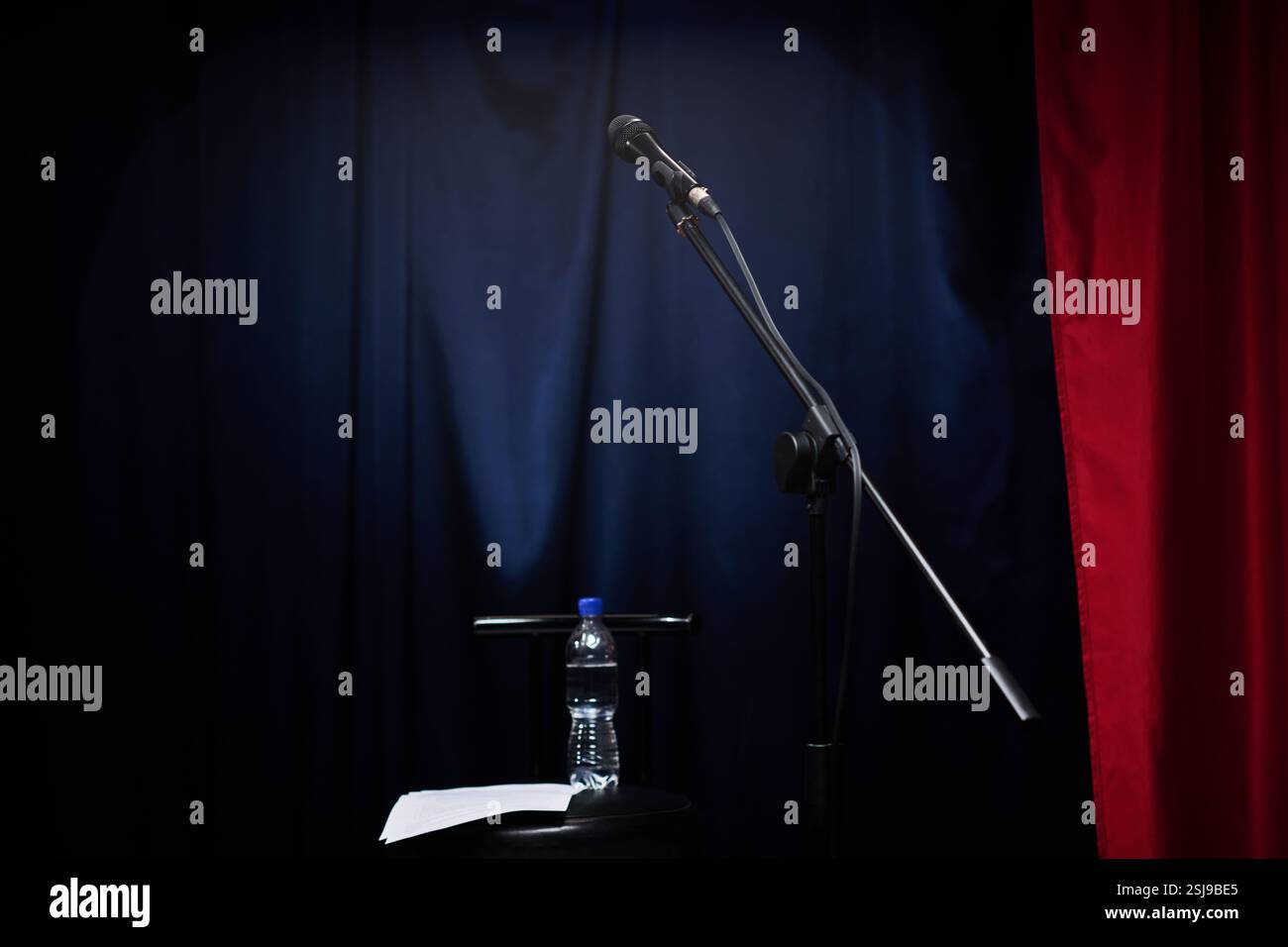 Microphone on stage with red curtain backdrop and a water bottle on ...