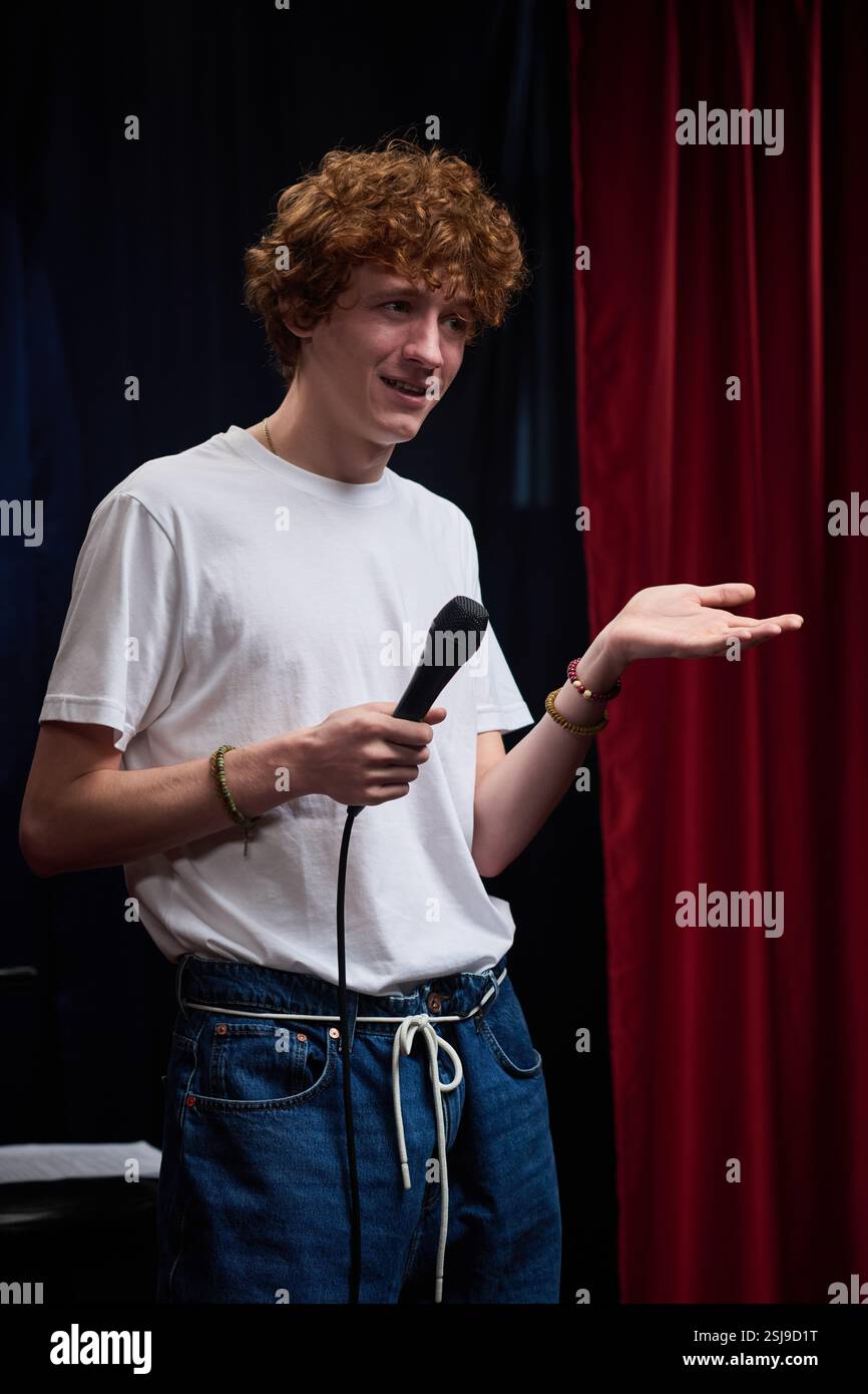 Person standing on stage holding a microphone, gesturing with hand and ...