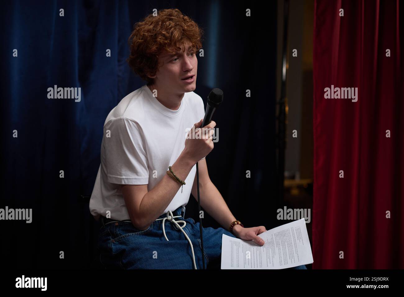 Young man holding microphone and script, performing on stage with ...