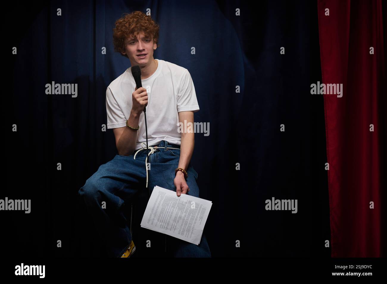 Young man standing on stage with paper and microphone performing comedy ...