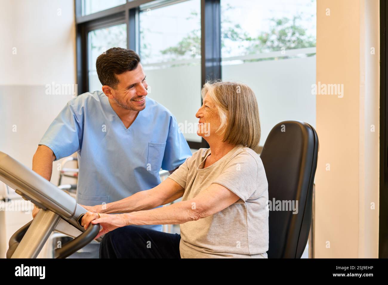 A smiling healthcare worker helps a senior woman use exercise equipment ...