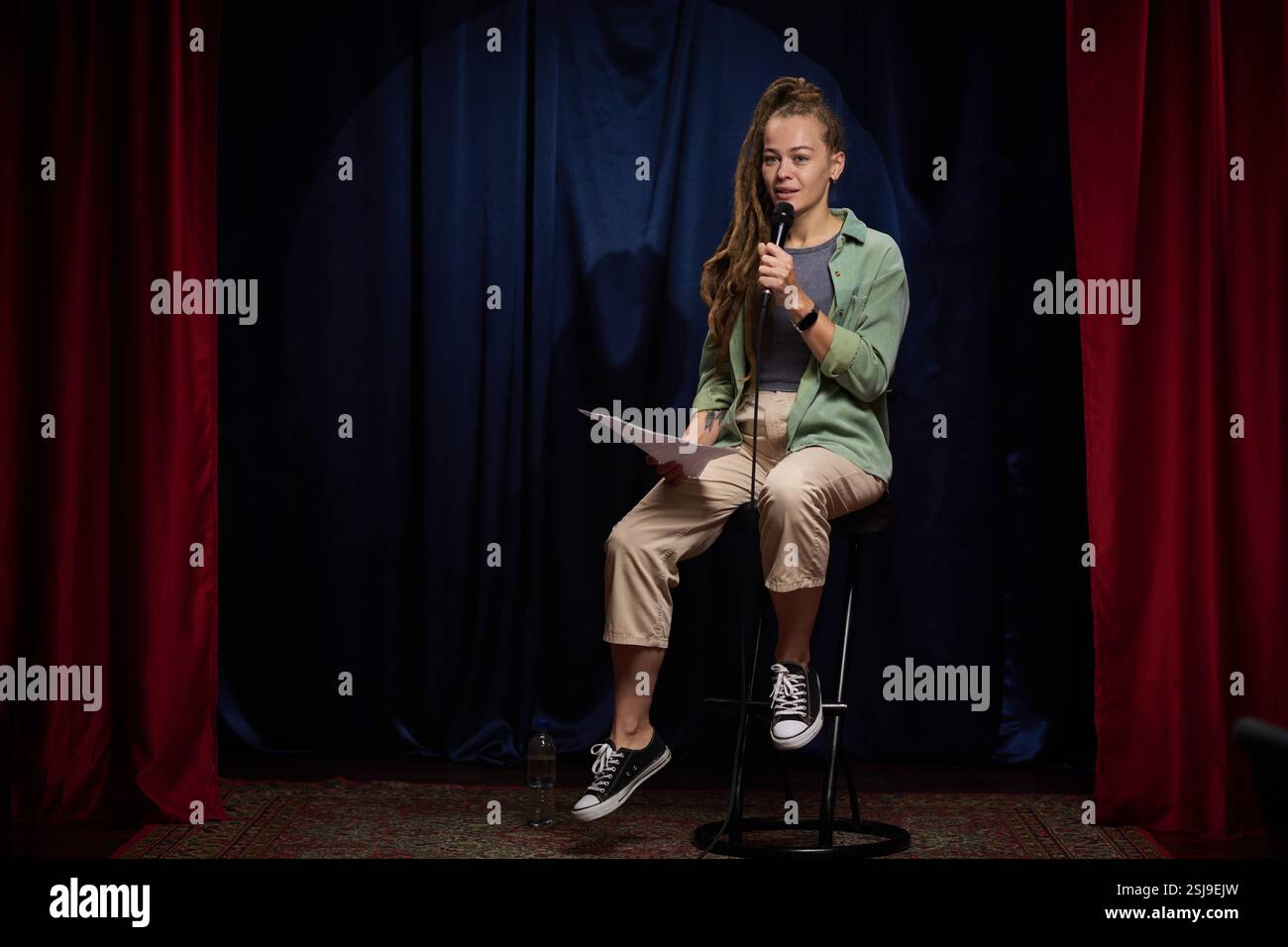 Young woman performing stand-up comedy on stage under spotlight while ...