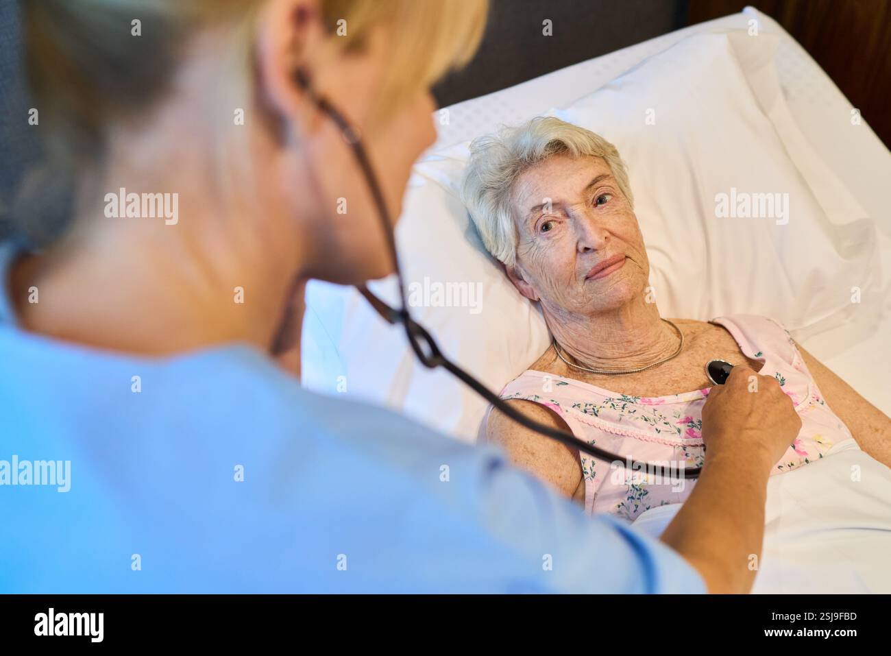 An elderly woman lying in a hospital bed receives attentive care from a ...