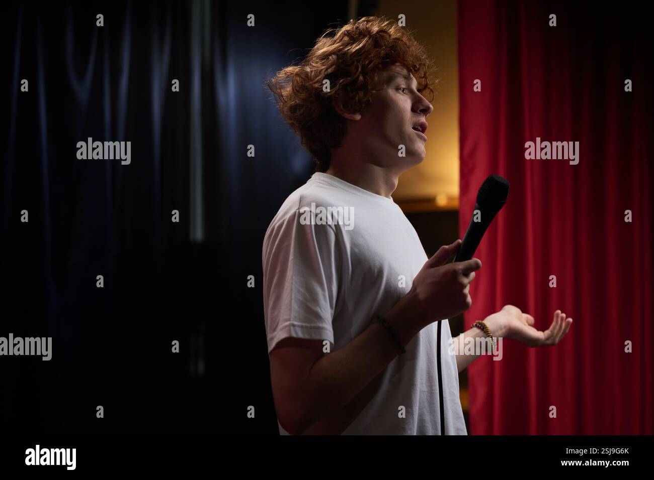 Young man standing on stage and speaking into microphone while ...