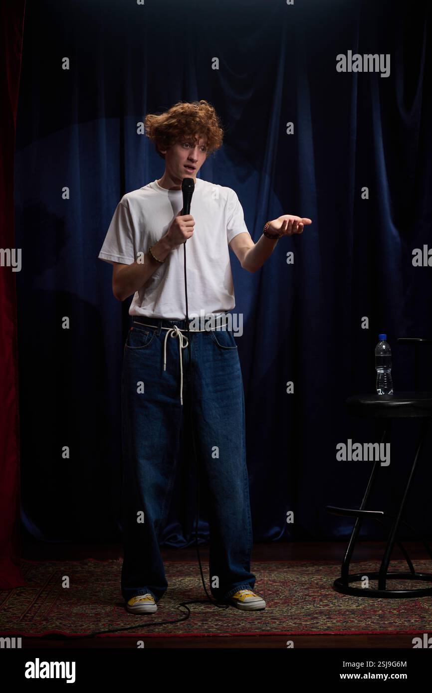 Young comedian delivering a standup performance on stage while holding ...