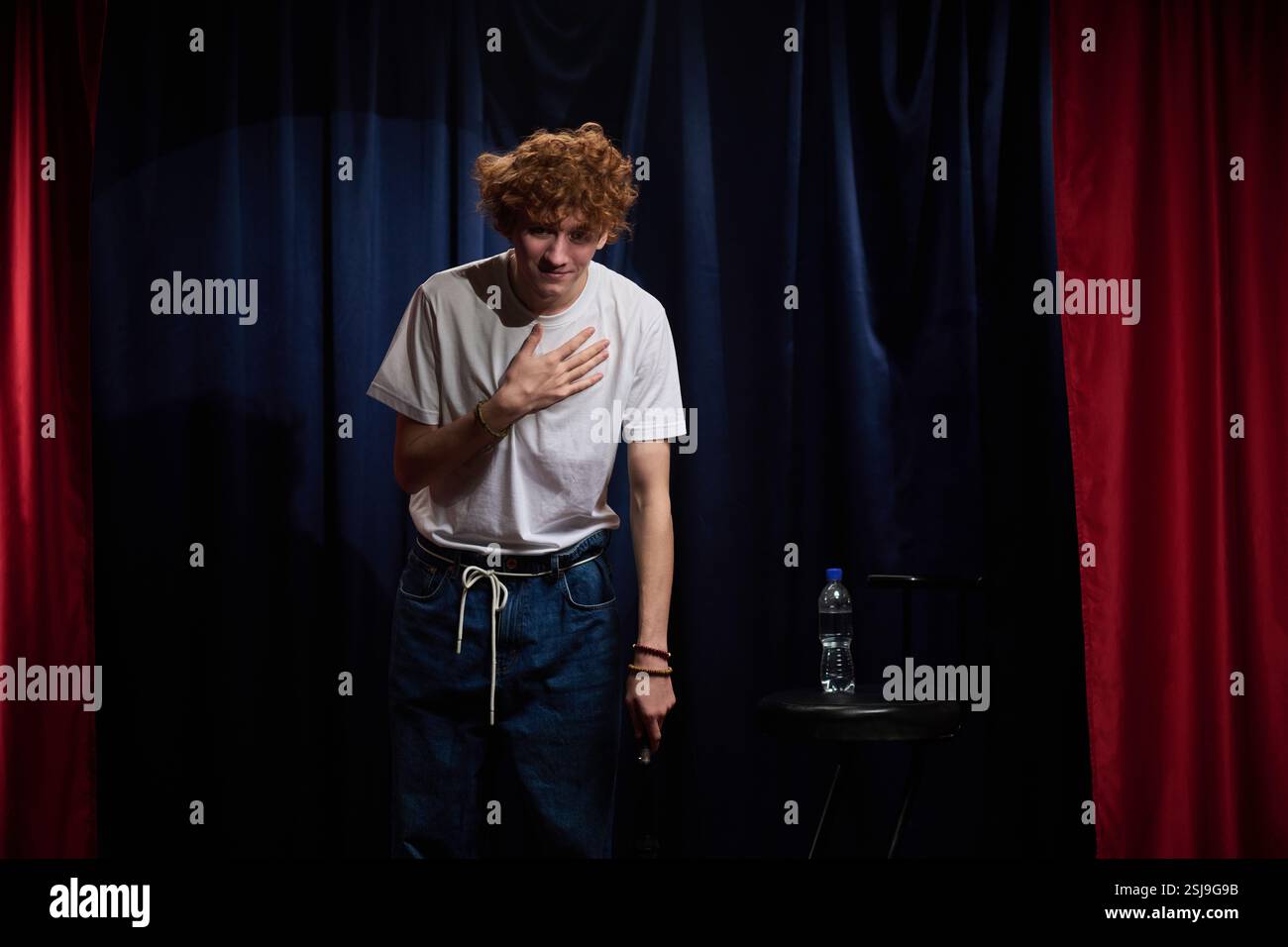 Person performing stand-up comedy, holding chest with one hand, and ...