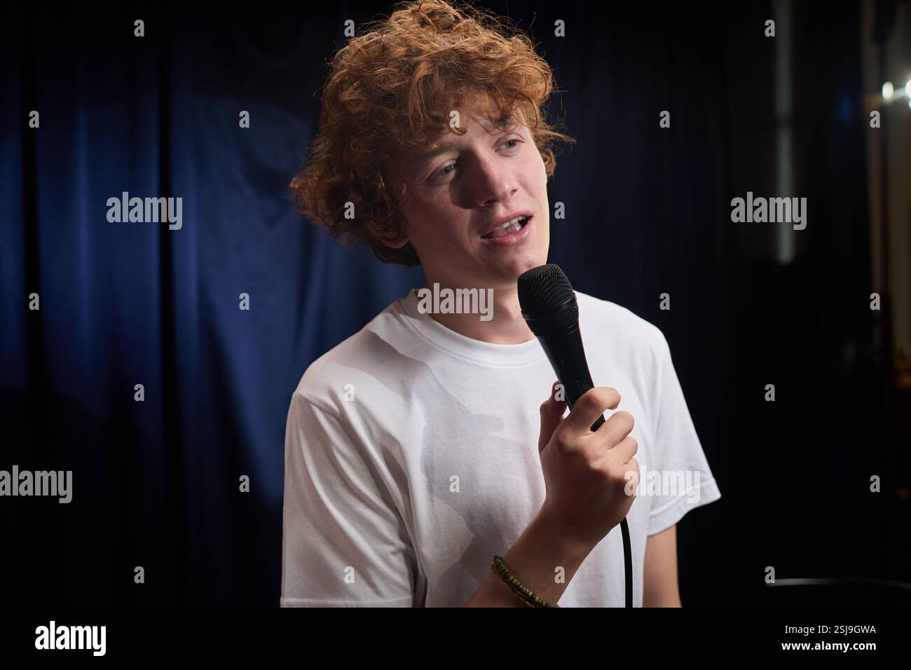 Young person singing during performance on stage, holding microphone ...