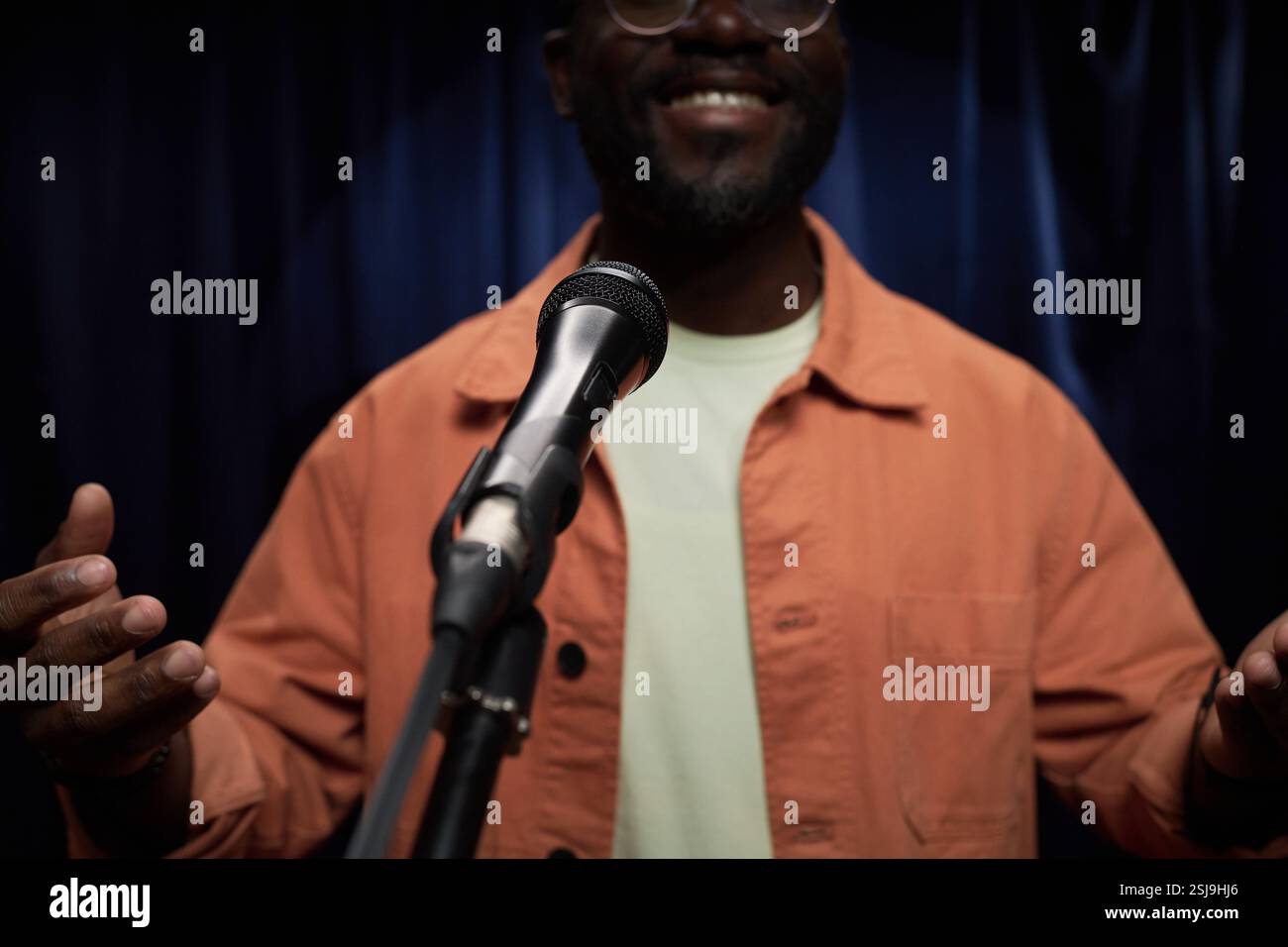 Comedian in a dark venue holding microphone and performing for audience ...