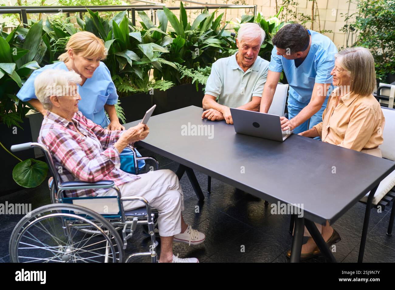 Outdoor setting with seniors and caregivers enjoying digital devices ...