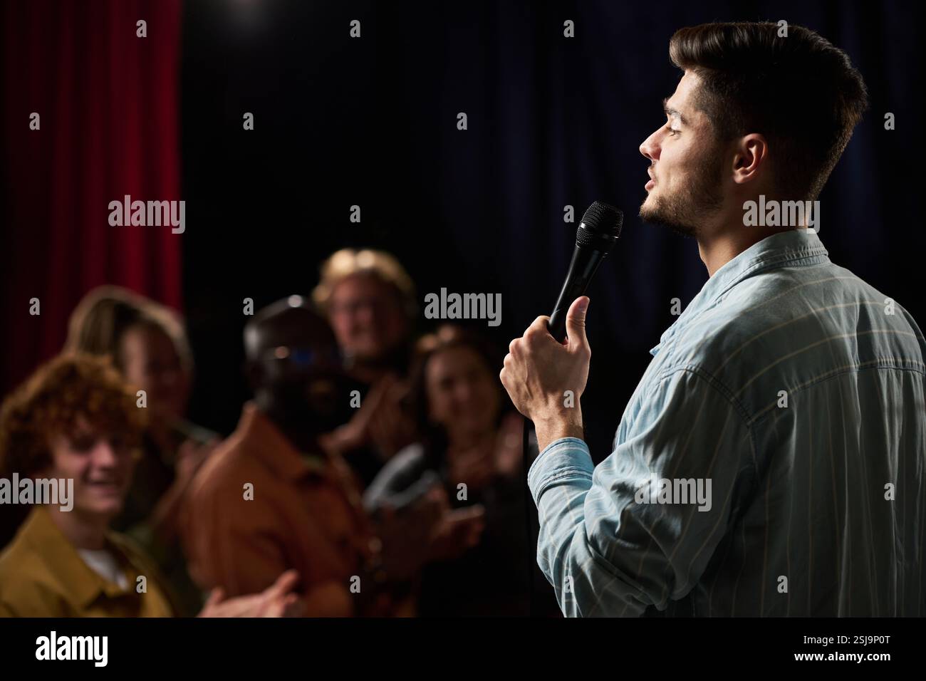 Man performing with microphone on stage in front of diverse audience ...