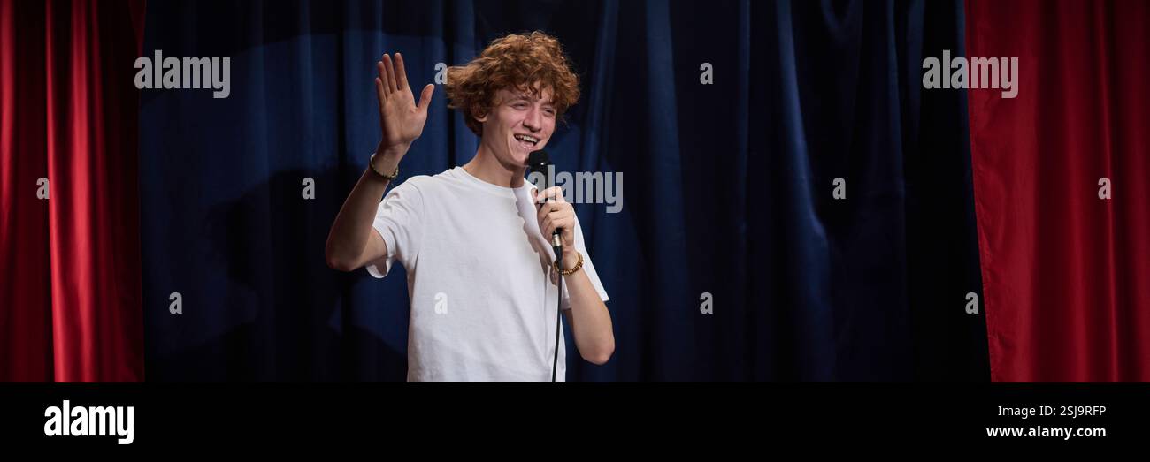 Young man performing stand-up comedy, smiling while holding a ...