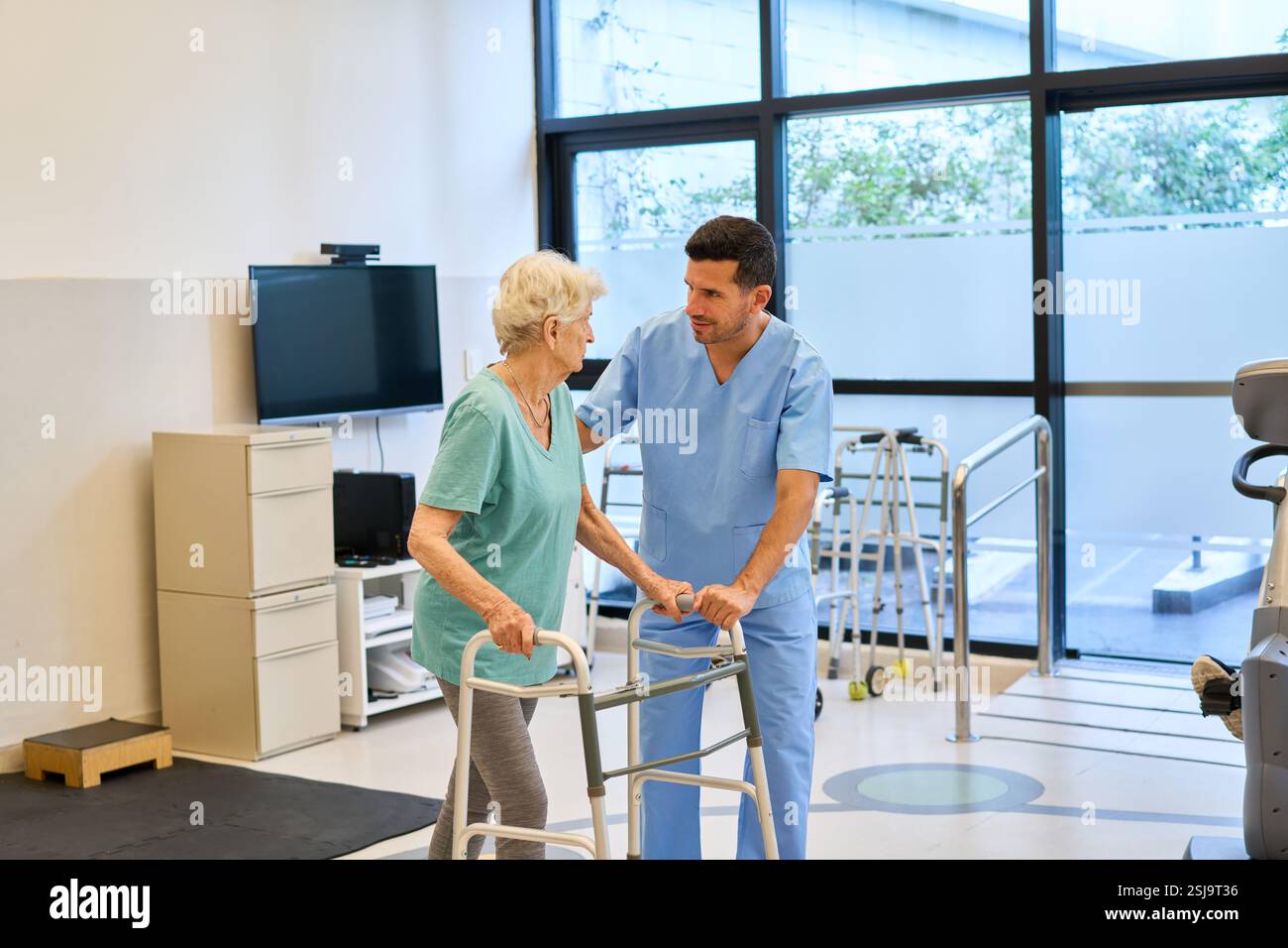 A physical therapist assists a senior woman using a walker in a rehabilitation facility ...