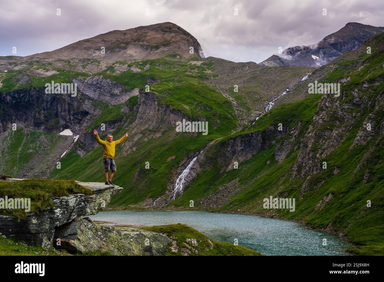 Happy man standing on rock, hands up and admiring majestic mountain ...