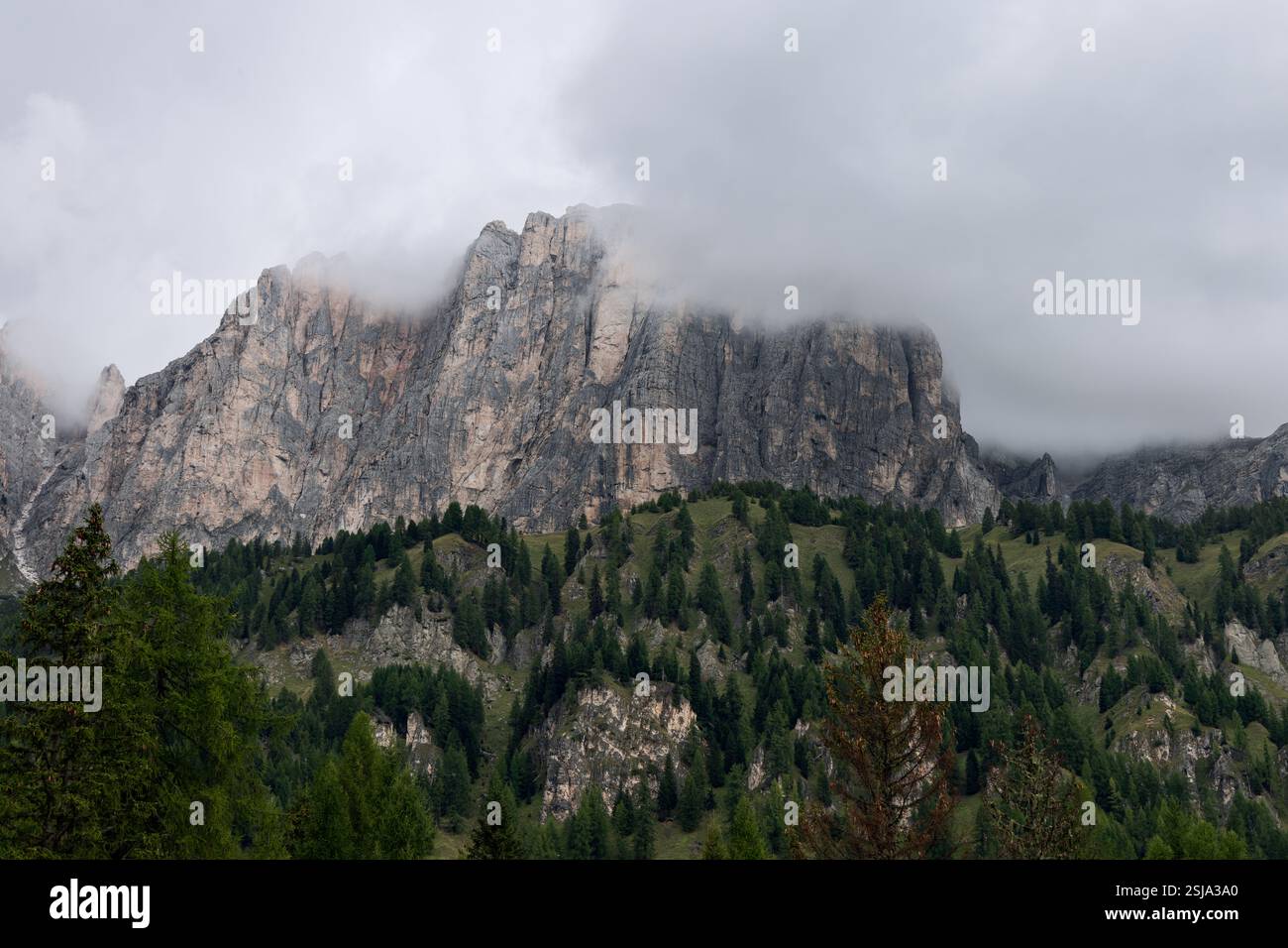 Clouds cling to the towering cliffs of the Dolomites, partially veiling ...