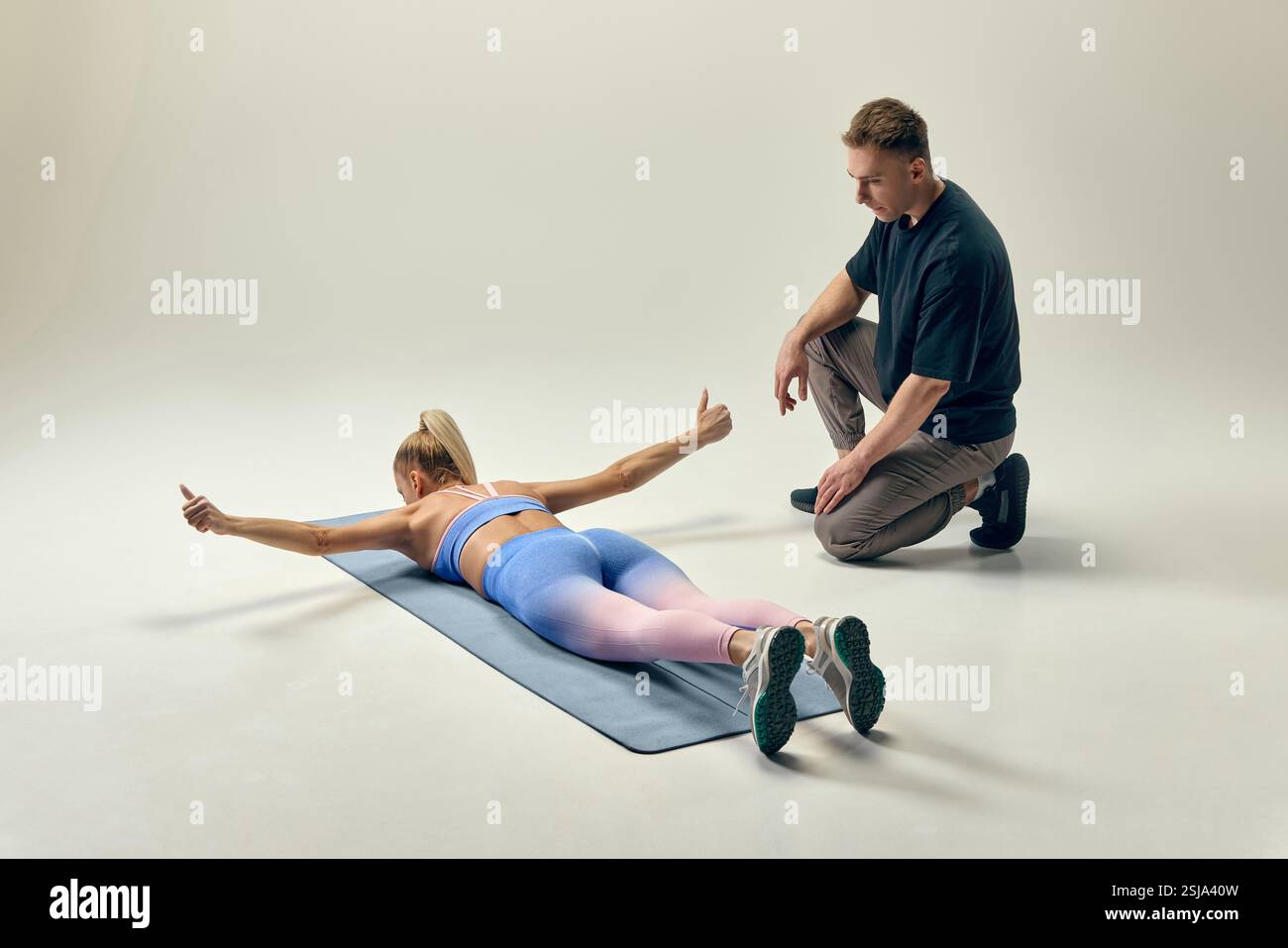 Woman lying on stomach performing back extension exercise, lifting arms ...