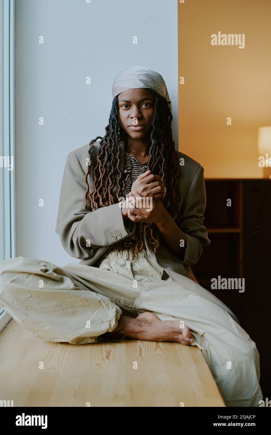 Portrait of African American woman sitting cross-legged near window ...