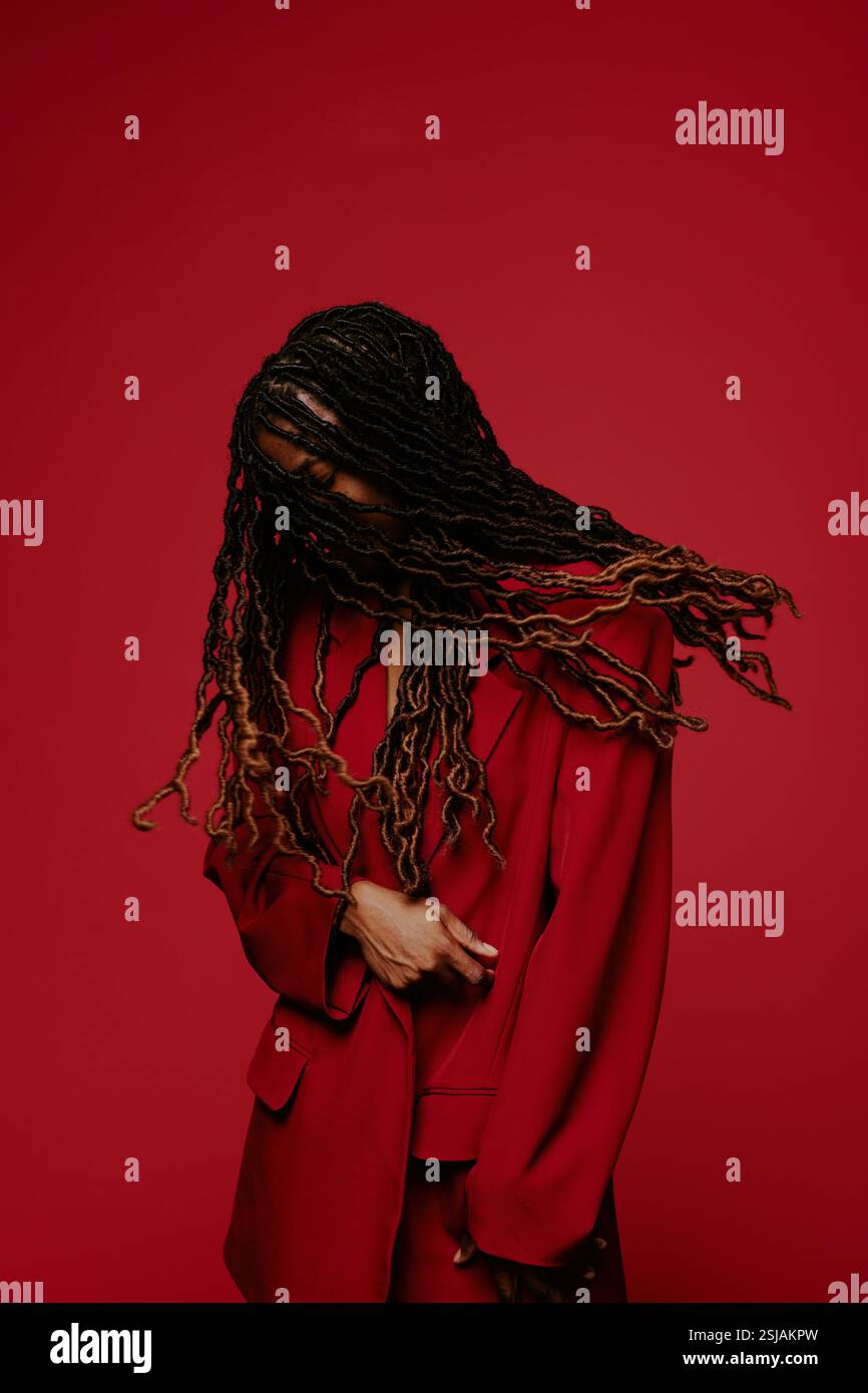 Individual wearing stylish all-red suit with long flowing braids covering face standing in front ...
