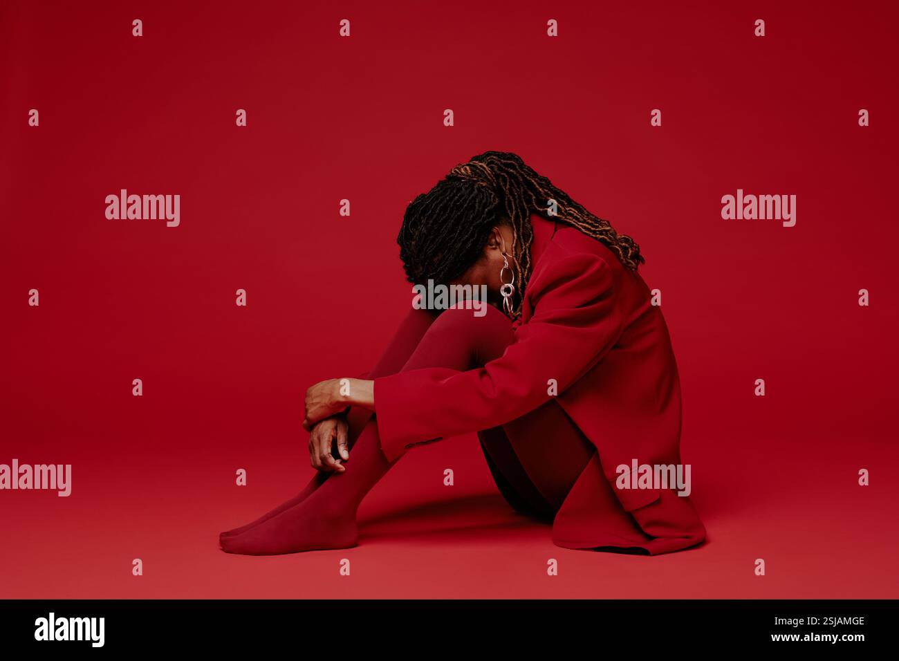Woman with braided hair sitting on floor, wearing red jacket and pants ...