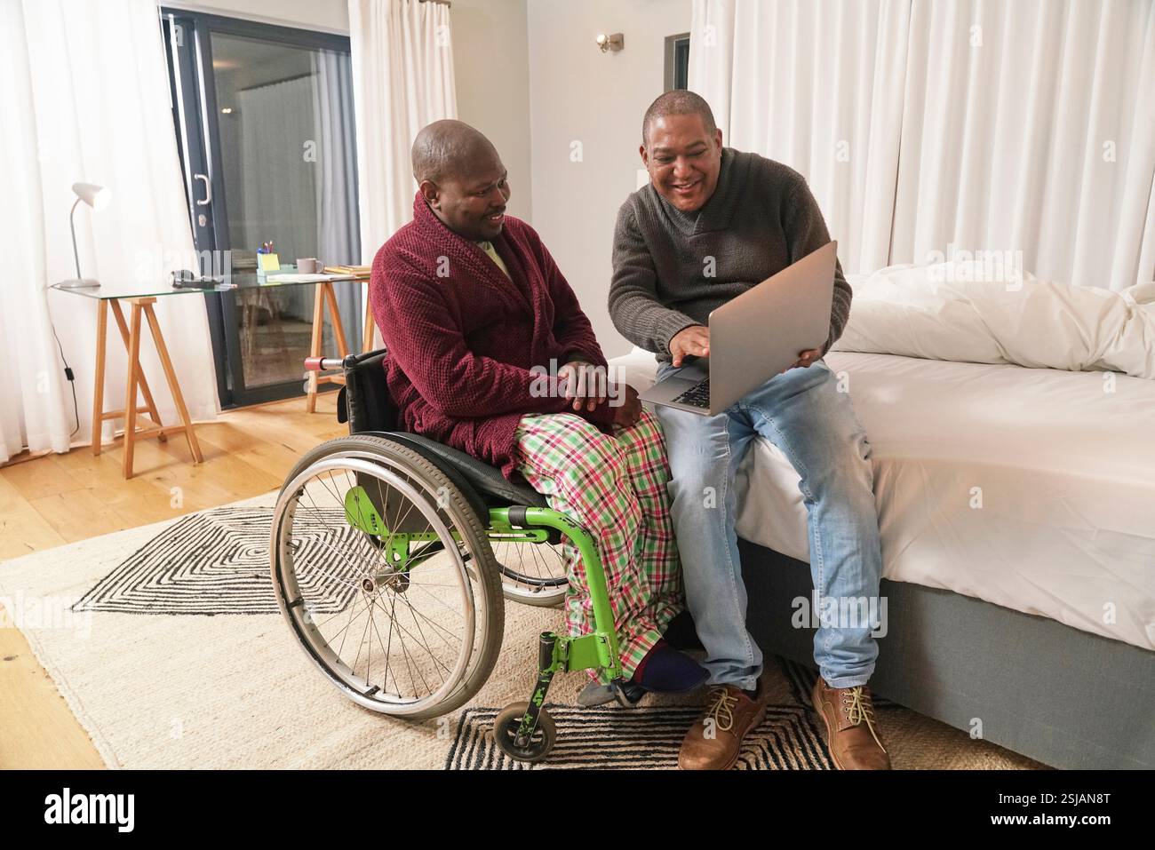 Man in wheelchair and his assistant using tablet in bedroom Stock Photo ...