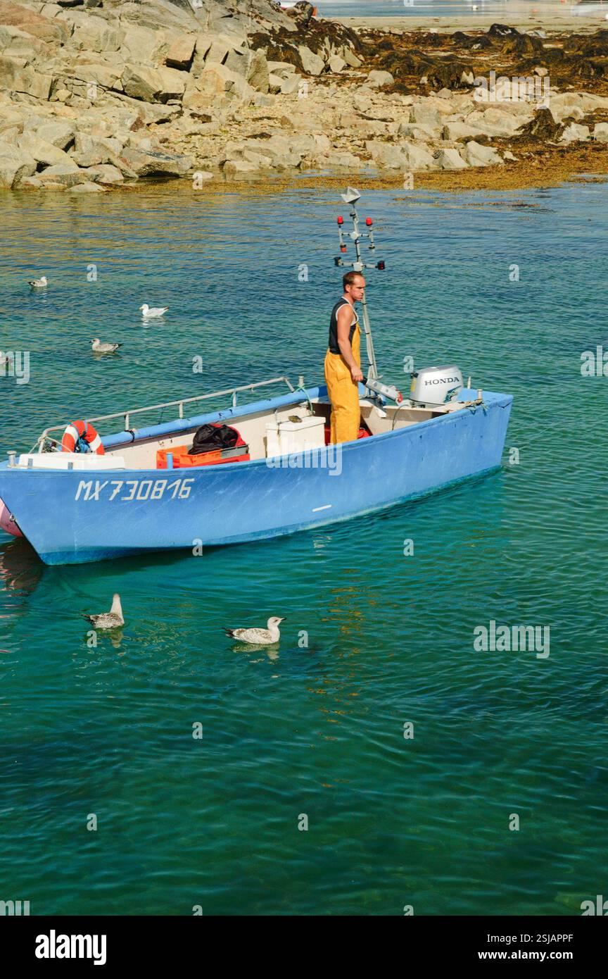 A man wearing orange overalls stands in a blue boat looking across the ...