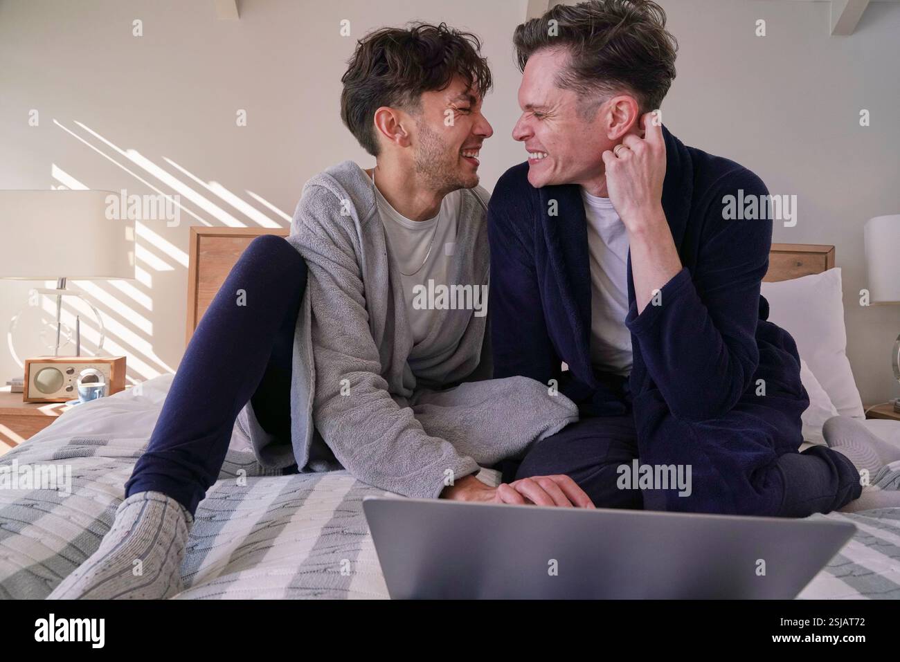 Happy gay couple with laptop on bed Stock Photo - Alamy