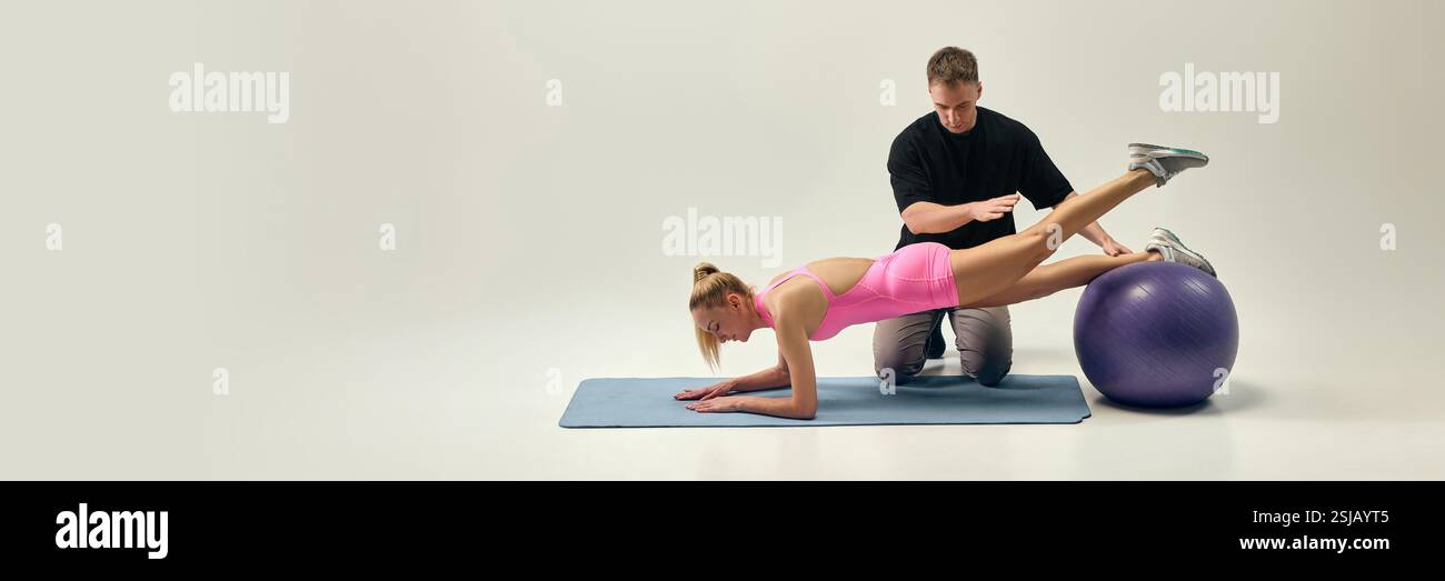 Trainer supporting woman performing plank with stability ball, ensuring ...