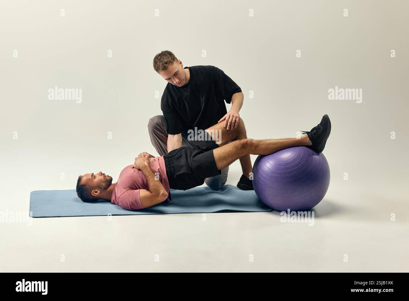 Trainer guiding man in bridge exercise with stability ball, ensuring ...